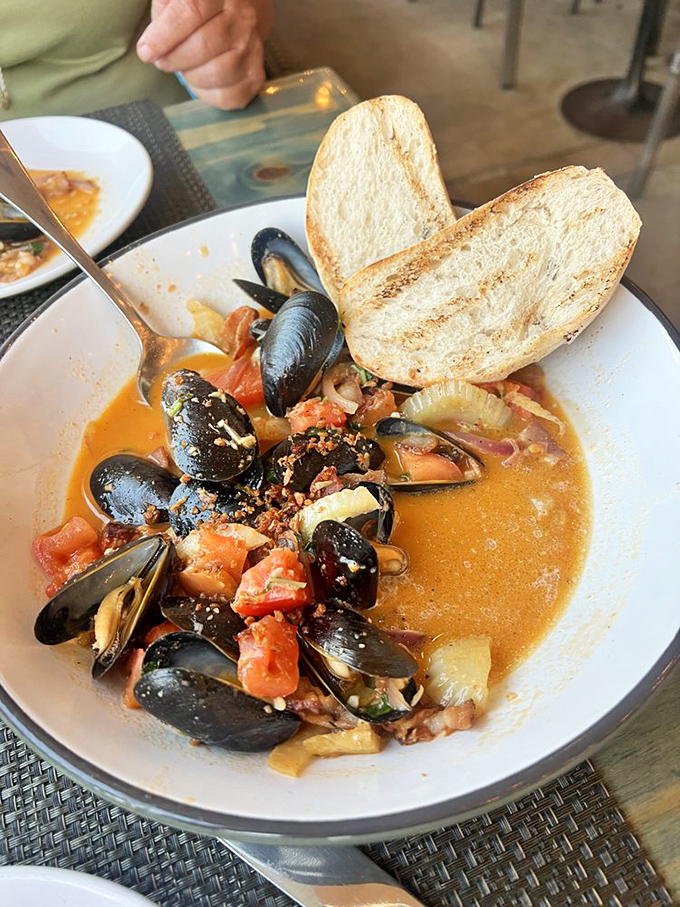 These mussels aren't just swimming in broth—they're luxuriating in a flavor hot tub that demands to be sopped up with every available bread surface.