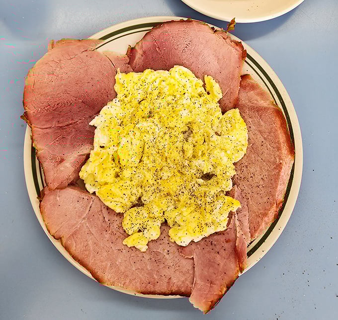 The famous ham and eggs breakfast presents like a sunflower—golden scrambled eggs surrounded by pink petals of thinly-sliced ham. Morning perfection on a plate.