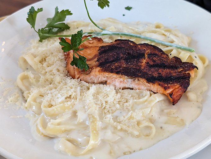 Blackened salmon over fettuccine—where smoky spice meets creamy indulgence. The parsley isn't just decoration; it's nature's way of saying "you're welcome."