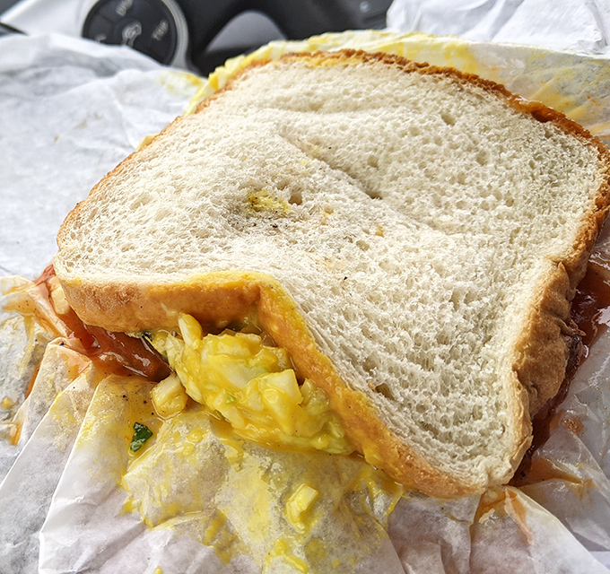 Not just any sandwich—layers of flavor architecture where bright mustard slaw meets smoky meat on a canvas of simple white bread.