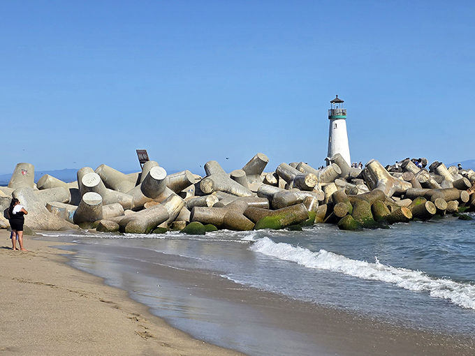 Where concrete meets sand meets sea. The lighthouse stands proudly as beachgoers enjoy California's greatest free entertainment—watching waves roll in endlessly.