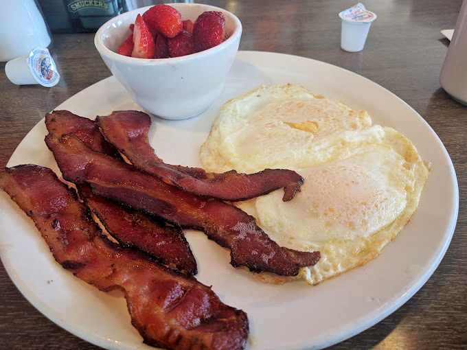 The breakfast trinity: crispy bacon, sunny-side-up eggs, and fresh strawberries—proof that mornings can actually be wonderful.