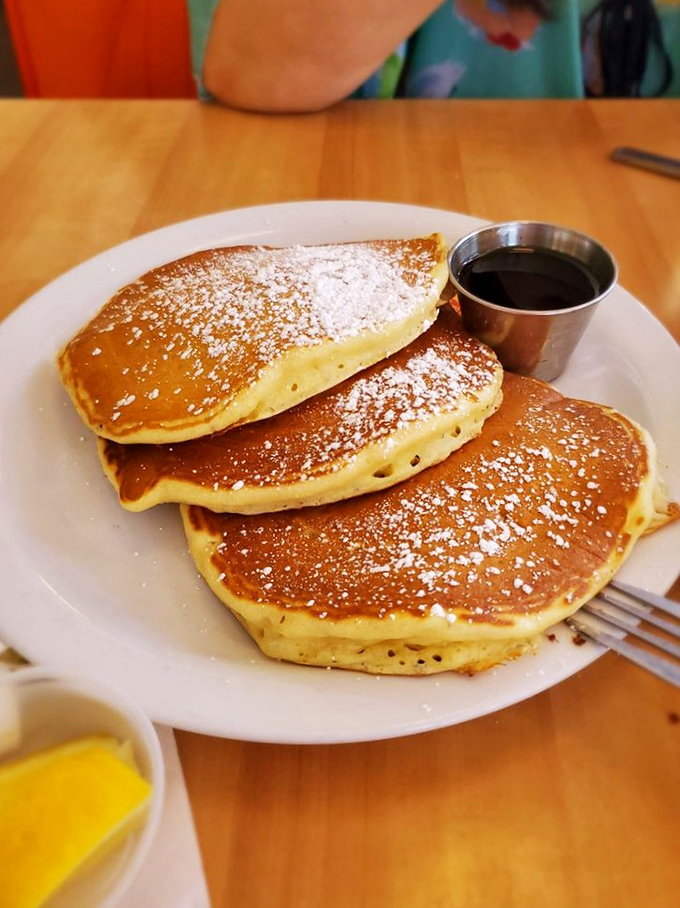 Pancakes with the perfect golden-brown hue and a dusting of powdered sugar. The tiny metal syrup pitcher is the crown jewel.