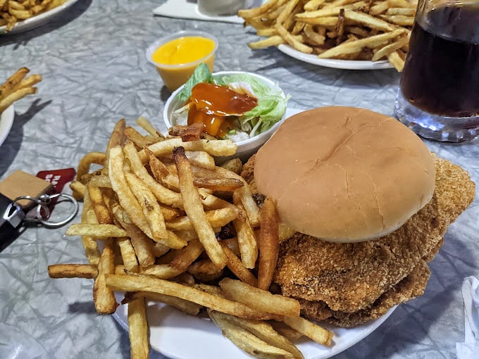 The pork tenderloin sandwich with golden-brown perfection extending well beyond its bun—a Midwest classic that demands a two-handed commitment.