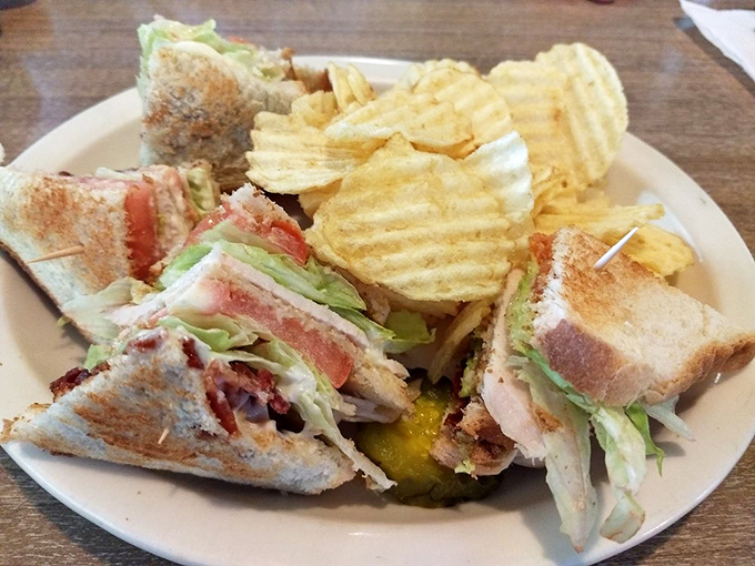 The club sandwich—architectural marvel of the diner world—stacked tall enough to require both hands and a strategic approach to each magnificent bite.