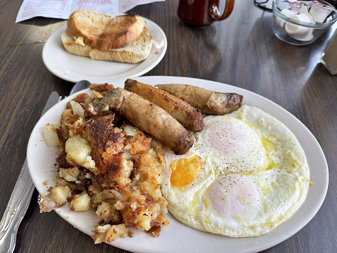 The holy trinity of breakfast comfort: perfectly sunny eggs, seasoned home fries with that ideal crisp-tender balance, and sausage links that snap with satisfaction.