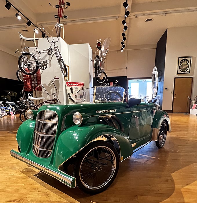 The green "Supercharge" vehicle demonstrates how bicycle technology influenced early automotive design—wheels before horsepower was even a concept!