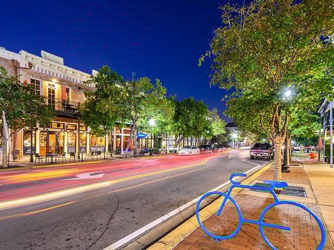 Vibrant nightlife in Pensacola's historic downtown district with tree-lined streets, outdoor dining, and a decorative blue bicycle sculpture.