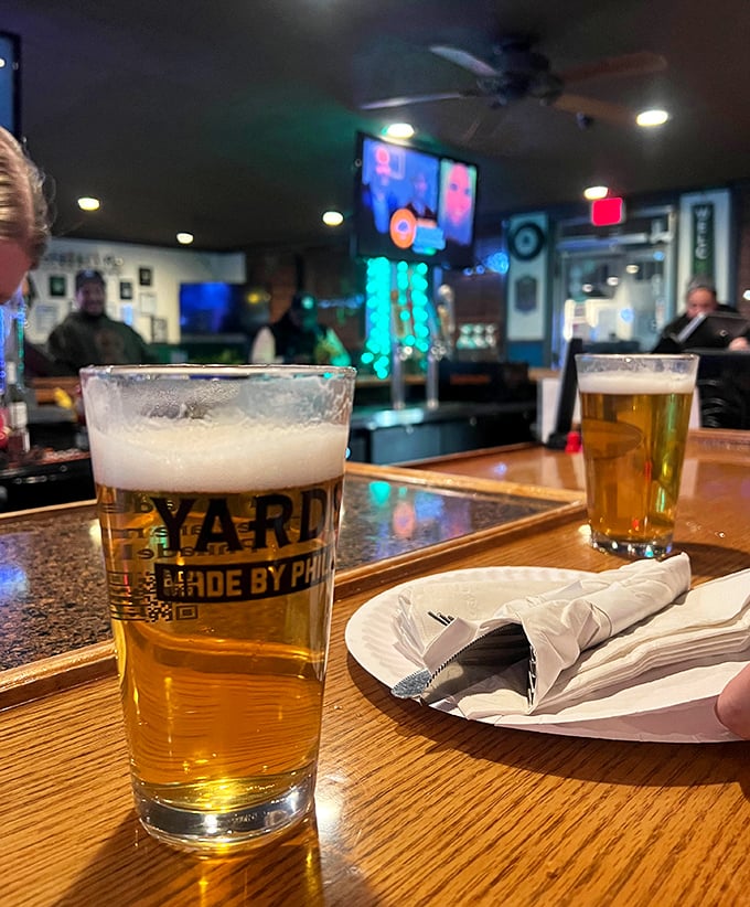 A perfectly poured pint sits on the bar top, foam crown intact. In the background, stories are being told, some of which might even be true.