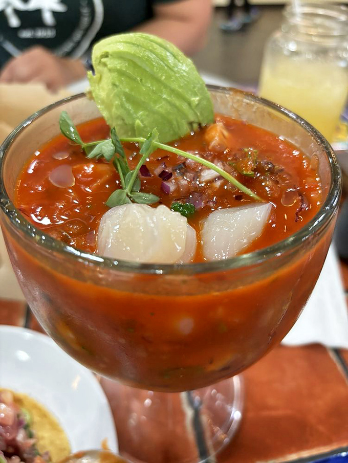A cocktail glass brimming with tomato-bathed seafood treasures—like a tiny ocean you can eat with a spoon.