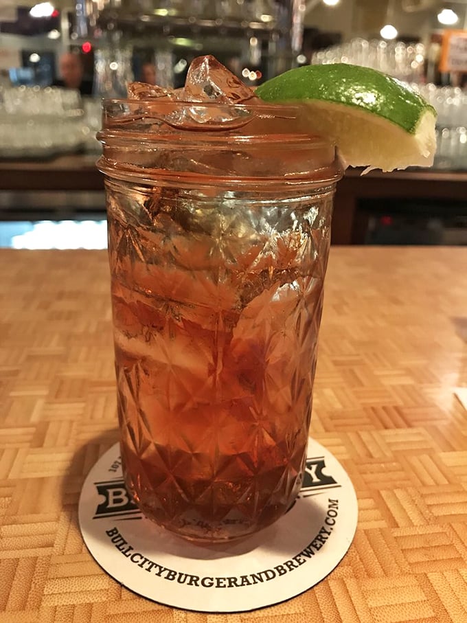 This isn't just a cocktail—it's liquid craftsmanship in a mason jar, garnished with lime and served on a coaster that reminds you exactly where this magic happened.