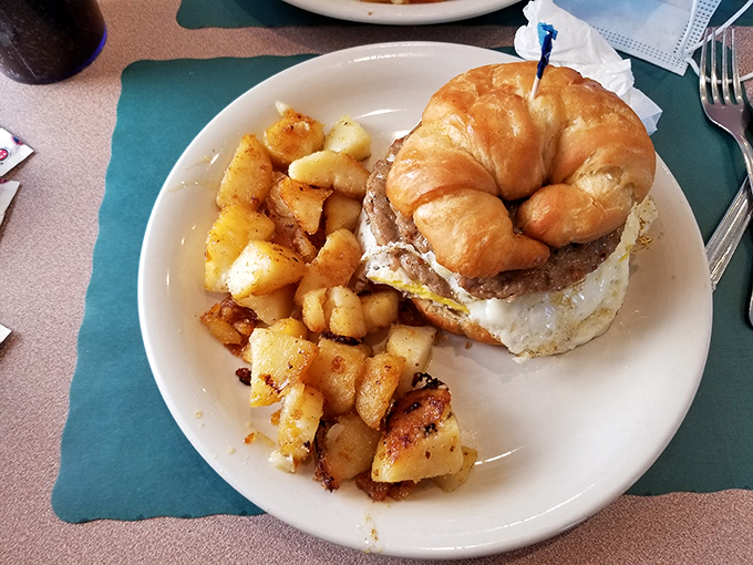 Breakfast gets the royal treatment when a buttery croissant becomes the throne for a perfectly cooked burger and egg—with home fries as loyal subjects.