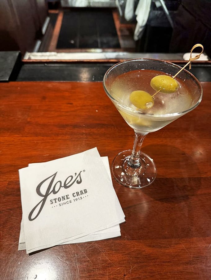 The martini sits regally on Joe's napkin—ice-cold, perfectly clear, with olives standing at attention like they know they're in the presence of greatness.