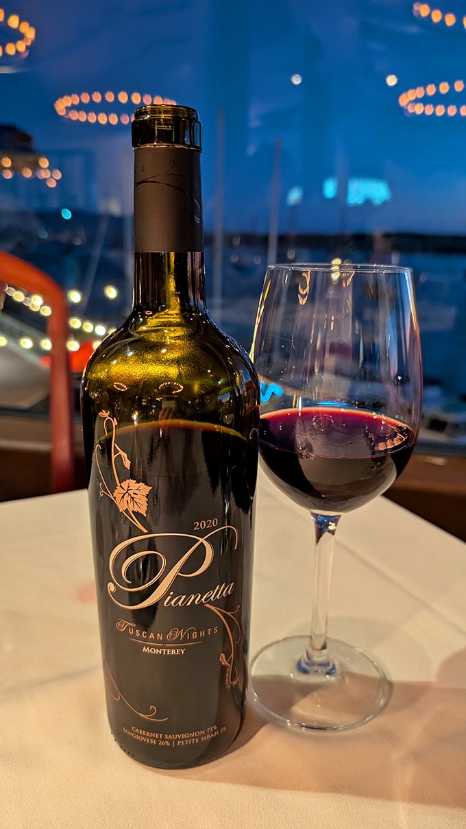 A glass of local red wine with the bay twinkling in the background—nature's perfect pairing for your seafood feast.