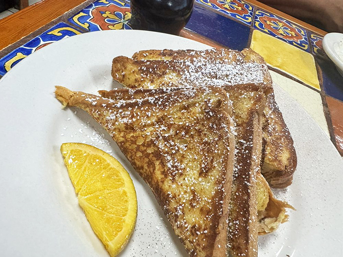 French toast that's dressed for success—golden-brown, dusted with powdered sugar, and ready for its close-up. That orange slice isn't just garnish, it's necessary brightness.