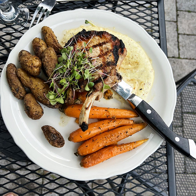 This pork chop isn't messing around—perfectly grilled and resting on a cloud of creamy sauce with colorful vegetables standing at attention alongside.