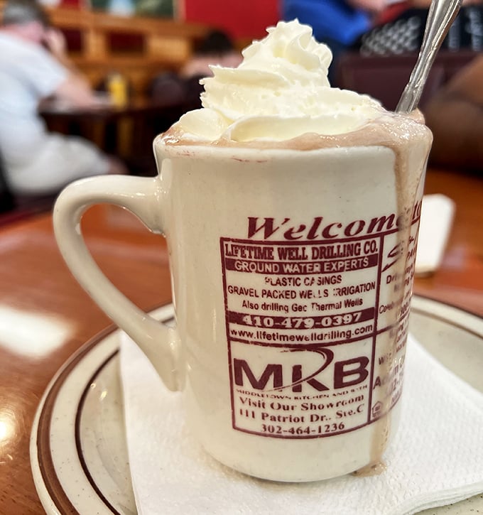 Hot chocolate that understands whipped cream isn't a topping—it's a lifestyle choice. The mug advertising local businesses is peak small-town charm.
