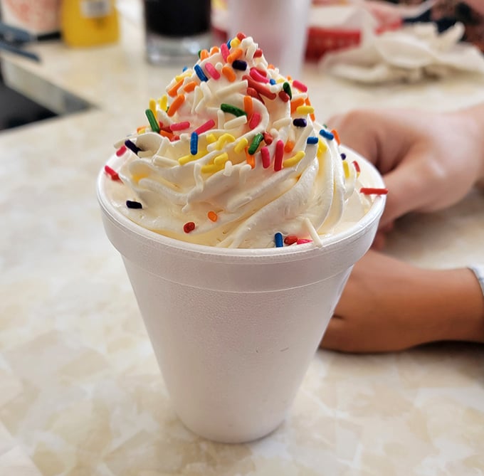 Whipped cream mountain with sprinkle confetti—this isn't just dessert, it's a celebration in a styrofoam cup that brings out your inner eight-year-old.