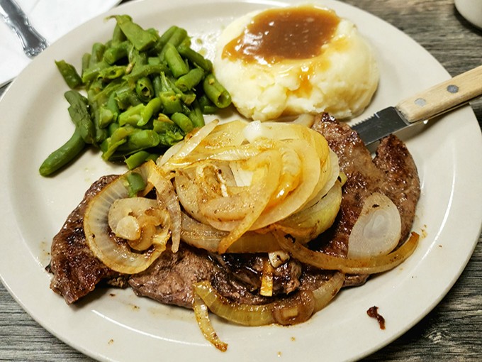 Tender steak topped with caramelized onions alongside perfectly cooked vegetables – proof that simple ingredients prepared well need no fancy embellishment.
