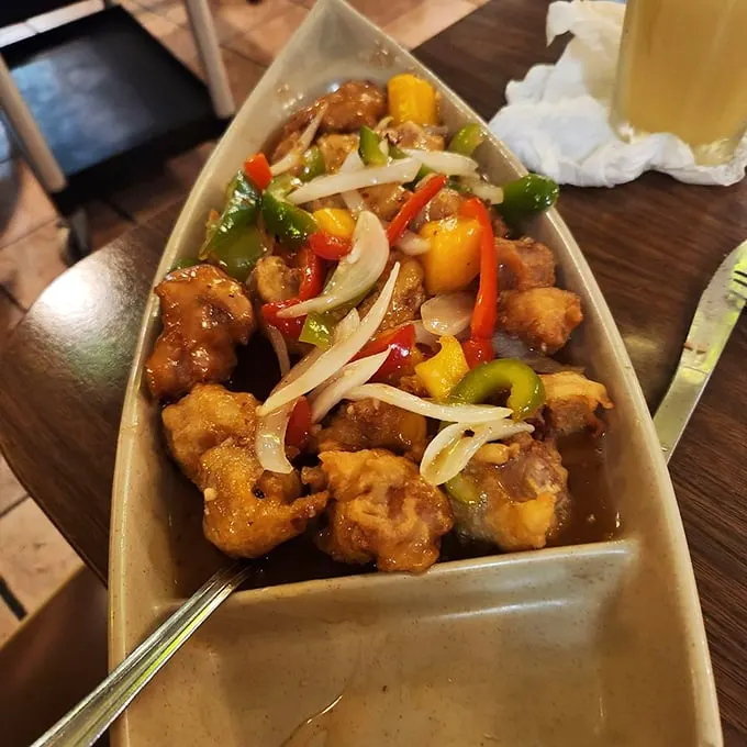 A boat-shaped vessel delivering tropical cargo—crispy pork with colorful peppers and onions that would make even a luau master nod in approval.