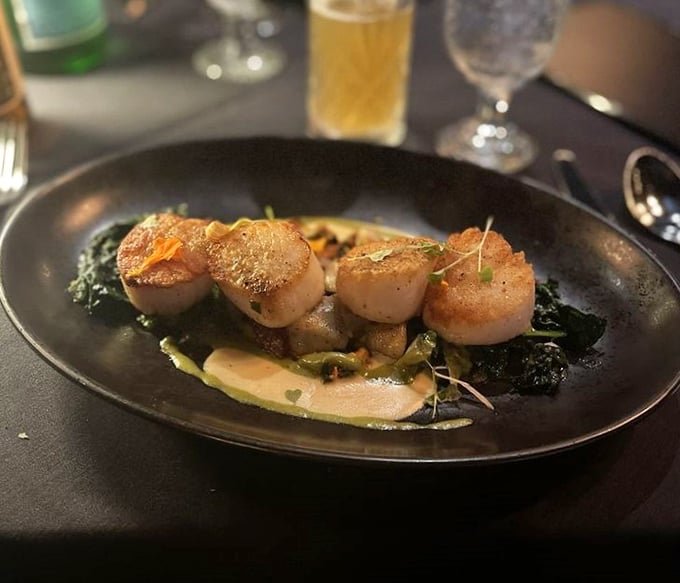Perfectly seared scallops perched atop vibrant greens—ocean treasures that have found their rightful throne on this sophisticated plate.