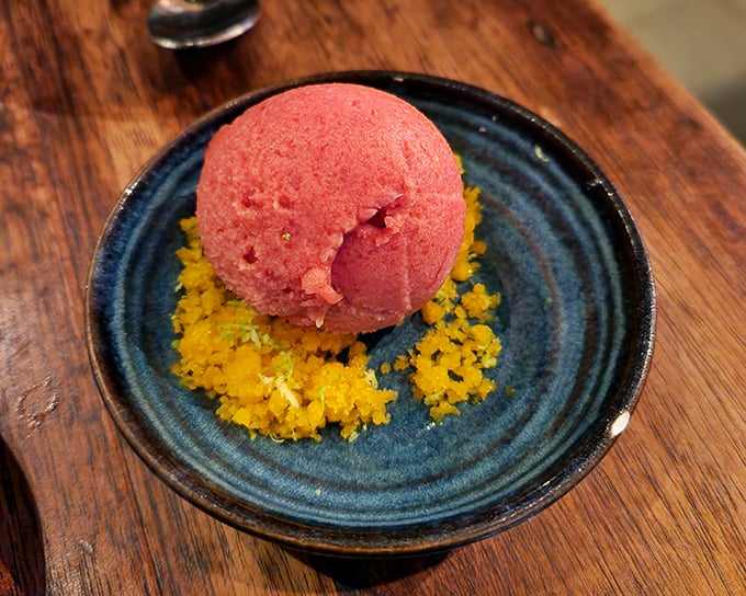A vibrant scoop of sorbet resting on sunshine-colored crumble—summer captured in a bowl, waiting to refresh your palate.