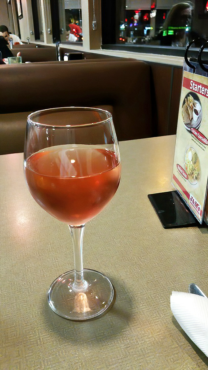 A glass of rosé sits elegantly beside the table menu, proving that unpretentious dining doesn't mean sacrificing life's little refinements. Wine not?