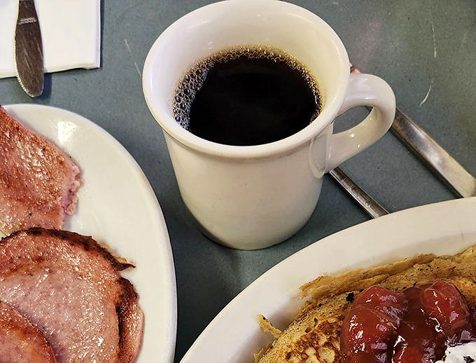 The diner coffee arrives in that perfect thick white mug—the kind that feels like shaking hands with an old friend.