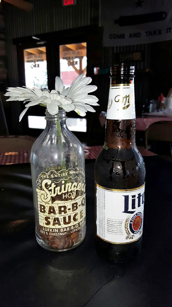 Every proper Texas meal deserves proper hydration—a repurposed sauce bottle becomes a flower vase while a cold beer stands at attention.