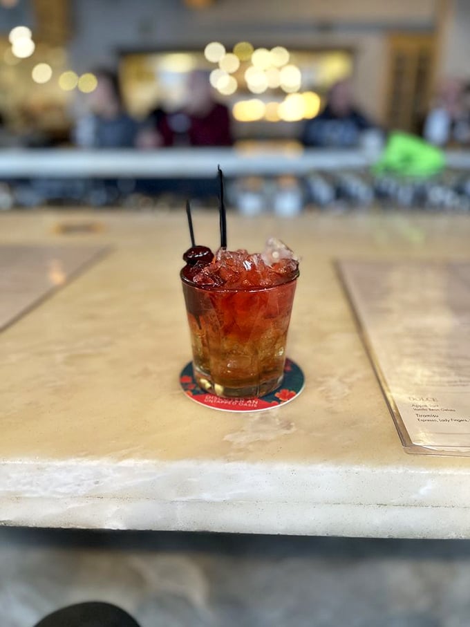 A cocktail that's dressed better than most people at the party, garnished with cherries that have clearly lived more interesting lives than we have.