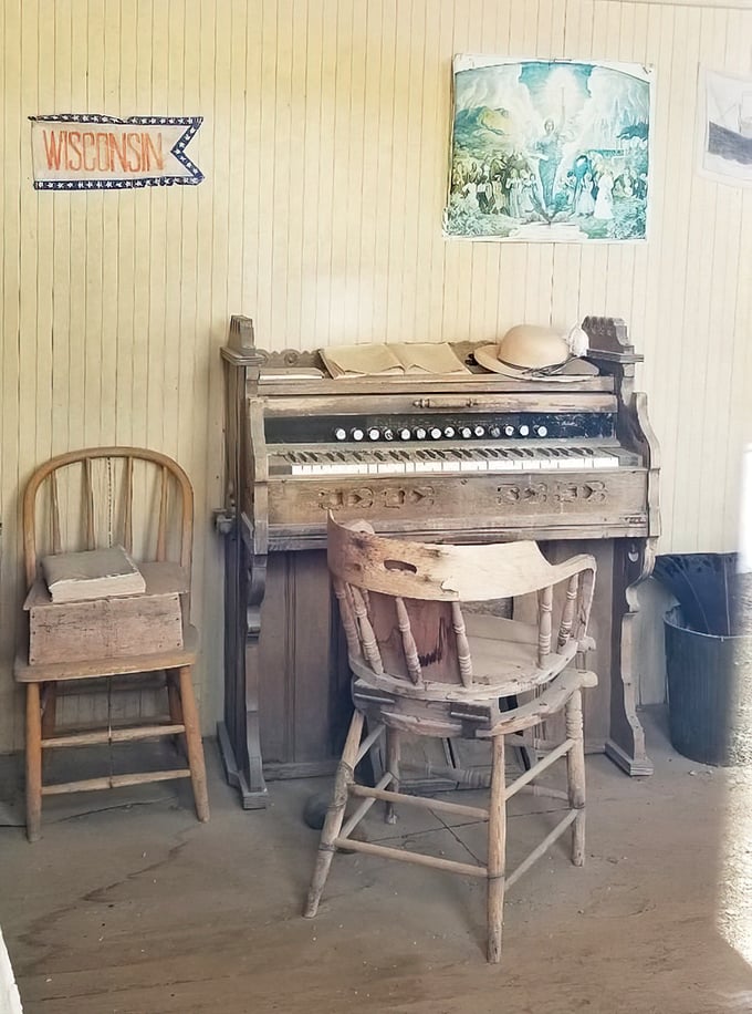 A dusty piano waits for phantom fingers, its Wisconsin banner hinting at dreams carried across the continent.