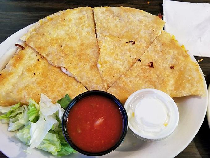 The quesadilla arrives with that perfect golden crisp, accompanied by the holy trinity of toppings—salsa, sour cream, and shredded lettuce.