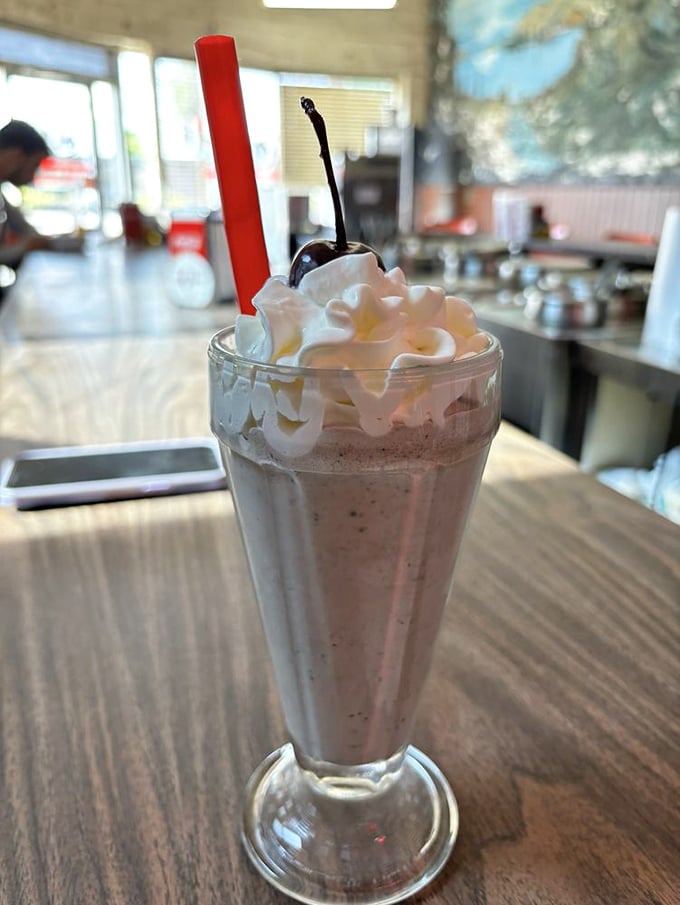 The milkshake arrives like a dessert from simpler times—whipped cream mountain, cherry on top, and that red straw promising sweet relief from the chili heat.