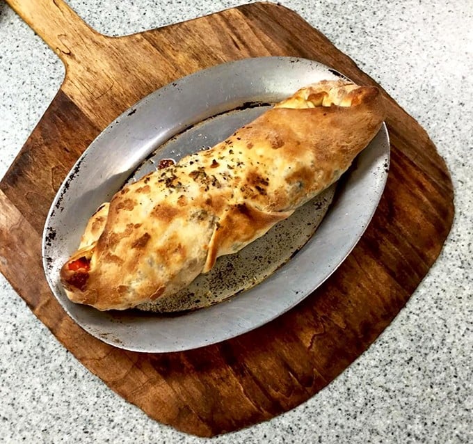 The stromboli—pizza's sophisticated cousin. Golden-brown exterior hiding a treasure trove of fillings, served on a metal plate that means business.