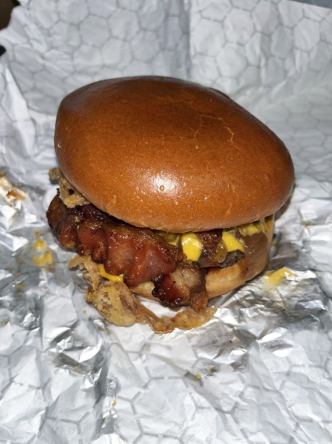This burger doesn't just sit on the plate—it lounges, confident in its bacon-crowned glory, practically winking at you from its foil throne. 