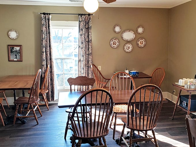 Sunlight streams through vintage curtains onto Windsor chairs and decorative plates—a dining room that feels more like coming home than eating out.