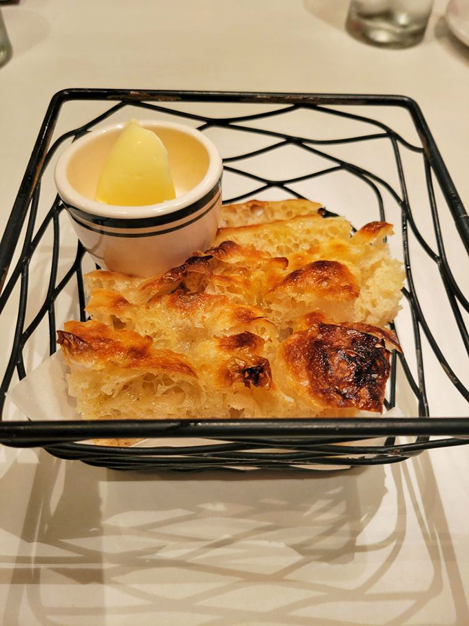 Focaccia that's achieved bread perfection—golden, airy interior with a crust that crackles just right, served with what appears to be honey butter.