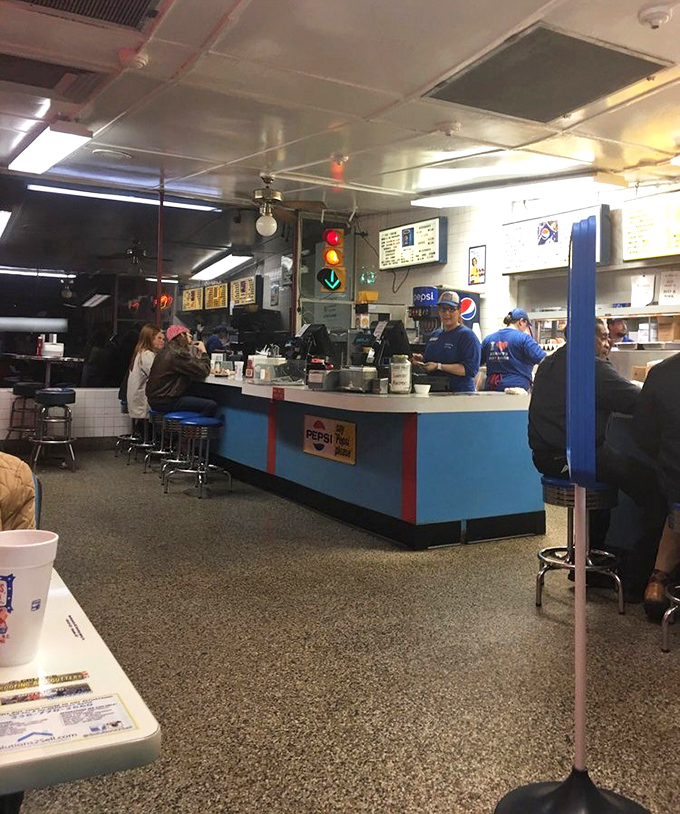 The counter where magic happens. Blue uniforms, efficient movements, and the symphony of sizzling meat create the perfect diner soundtrack that money can't buy.