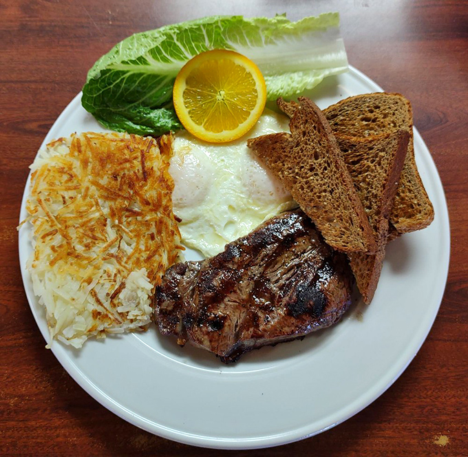 A breakfast classic ready for its close-up—perfectly grilled steak, sunny-side-up eggs, crispy hash browns, and rye toast with a slice of lemon for that unexpected twist.