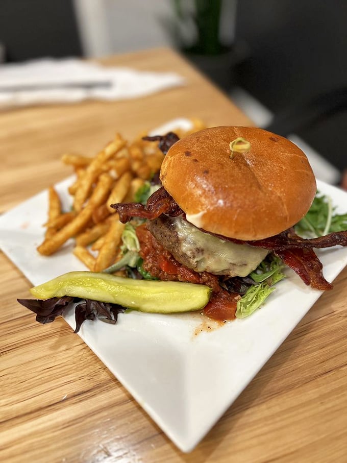 Burger architecture at its finest. A golden brioche bun cradling a juicy patty, crisp bacon, and melted cheese – with a pickle standing guard against mundane meals.