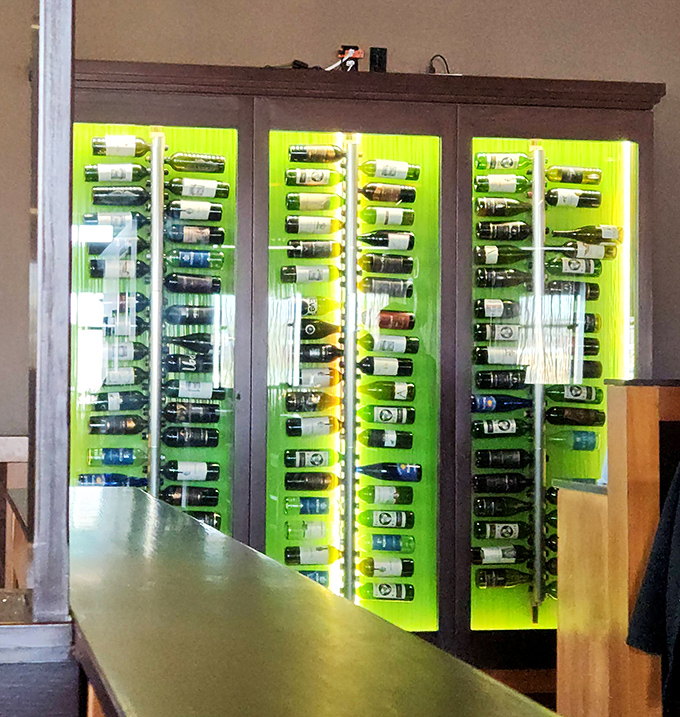 The wine display glows with emerald backlighting, showcasing bottles like precious artifacts in a museum of adult grape juice.