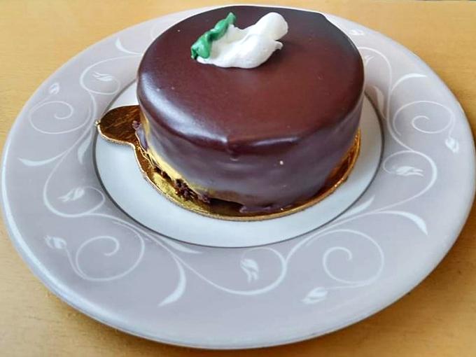A chocolate mousse cake so perfectly formed it seems to defy physics—the glossy ganache surface reflecting your expression of pure anticipation.