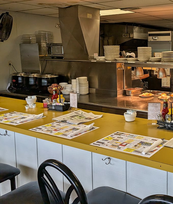 The counter seating offers a front-row view to the kitchen magic, where newspapers and coffee create the perfect morning ritual.