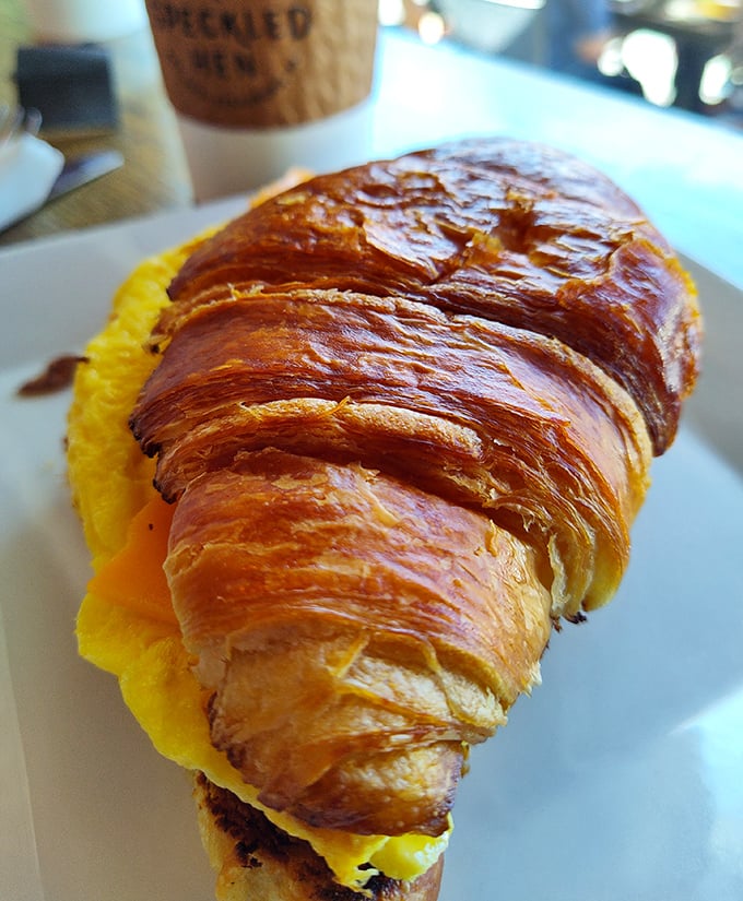 A croissant with serious intentions – buttery, flaky architecture cradling bright yellow eggs in a breakfast sandwich worth setting alarms for.