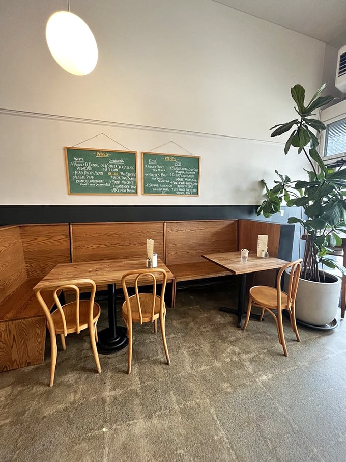 Plants climbing toward sunlight, wooden chairs awaiting conversations, and the promise of deliciousness on those perfectly set tables – this corner feels like breakfast therapy.