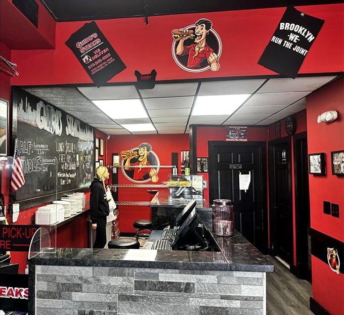 The counter where dreams come true. Red walls, stone facade, and a chalkboard promising "NEW SANDWICHES"—three syllables that spark joy.