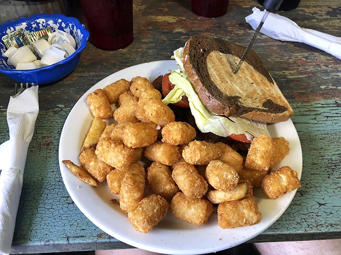 A sandwich surrounded by golden tater tots like crispy little bodyguards protecting the main attraction. Comfort food at its most comforting.