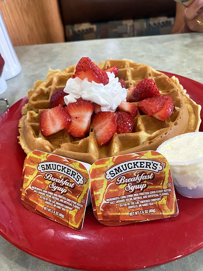 A waffle that's dressed for success with strawberries and whipped cream. Smucker's syrup standing by like eager understudies.