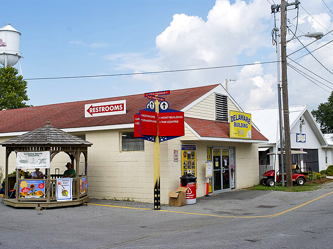 This image shows the Delaware Building at the Harrington Fairgrounds, with a gazebo, directional signs, and a water tower in the background.