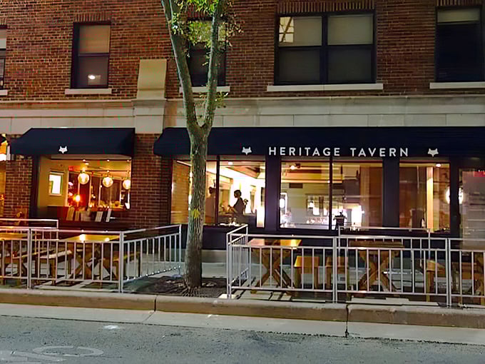 Heritage Tavern's brick façade glows with warm invitation as evening falls, its fox logo standing sentinel over Madison's culinary gem.